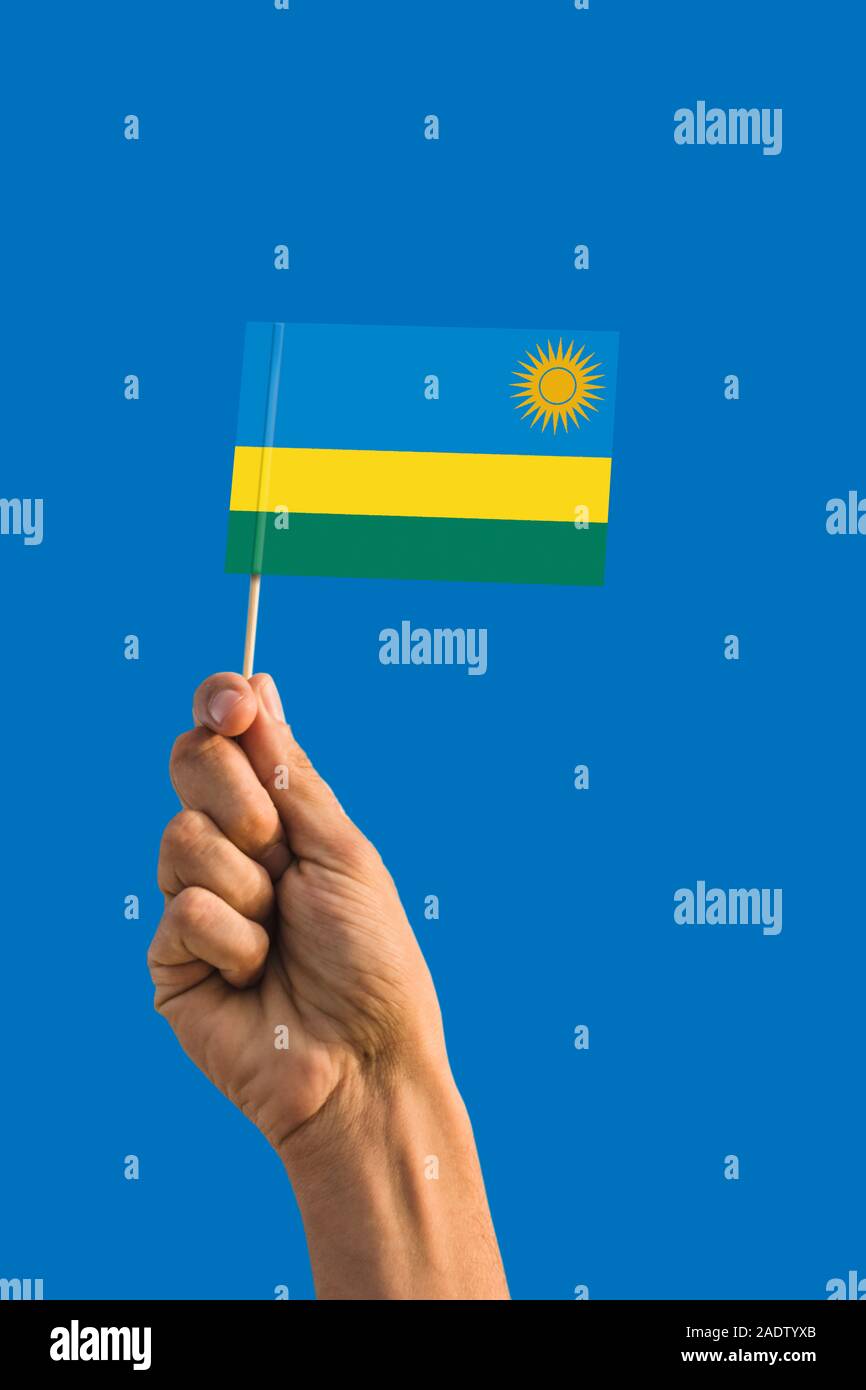 Woman hand holding Rwanda flag with stick, waving flag on deep blue sky ...