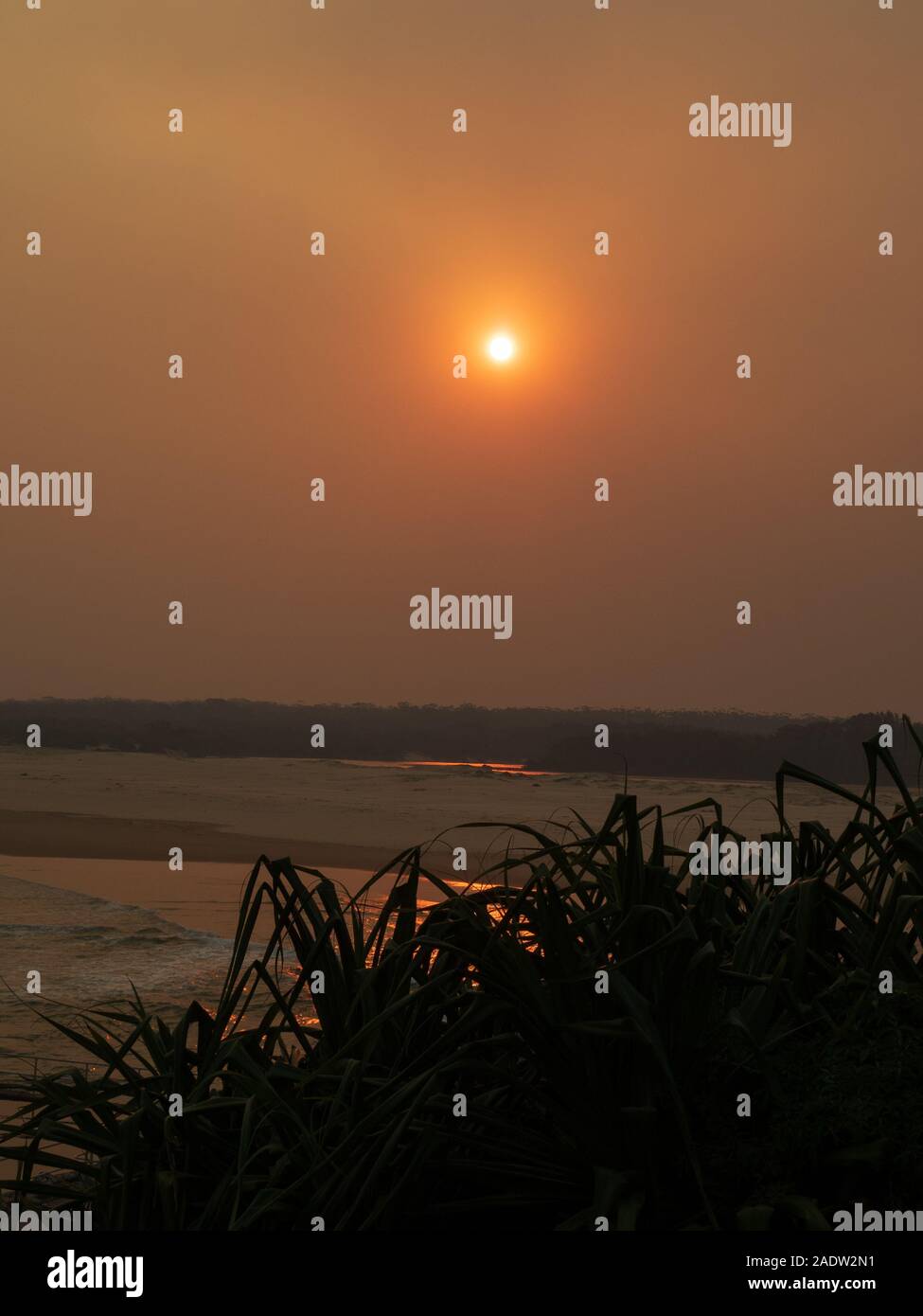 Smokey orange sun reflected in the ocean above the beach Stock Photo ...