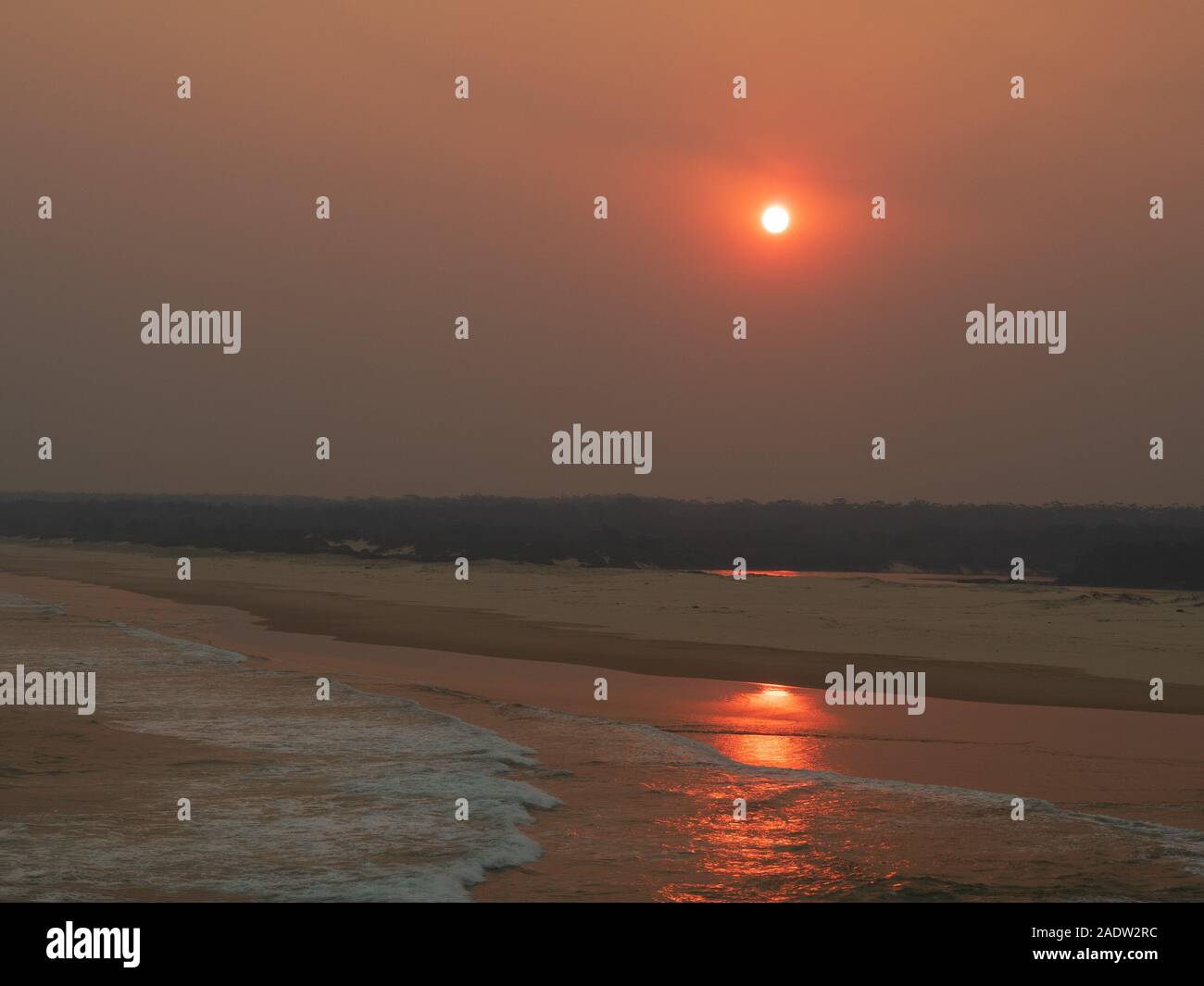 Smokey orange sun reflected in the ocean above the beach, Australian ...