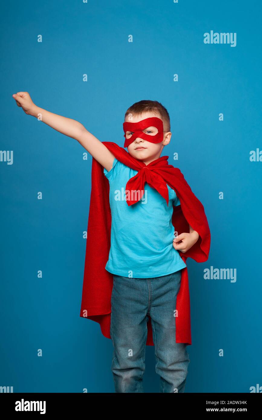 Boy in red superhero cloak on empty blue background Stock Photo - Alamy