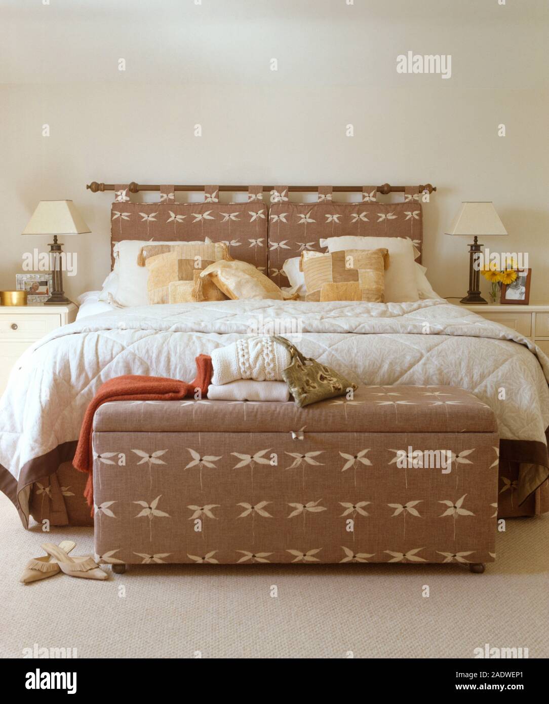 Upholstered rectangular ottoman chest below bed with beige cushions on ...