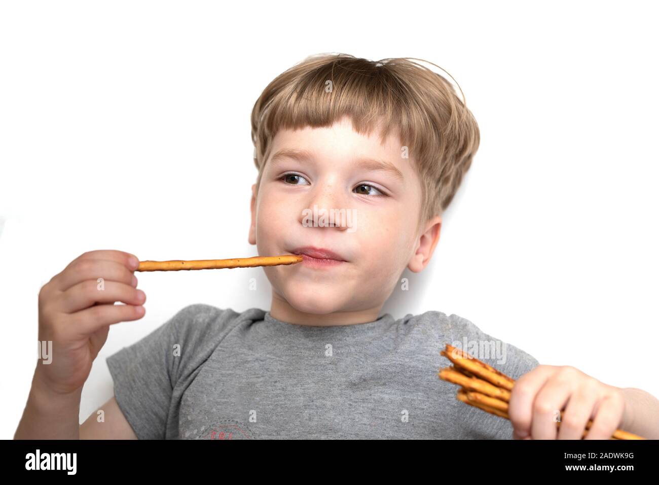 5 years old boy eats bread sticks on a white background, crispy snack ...
