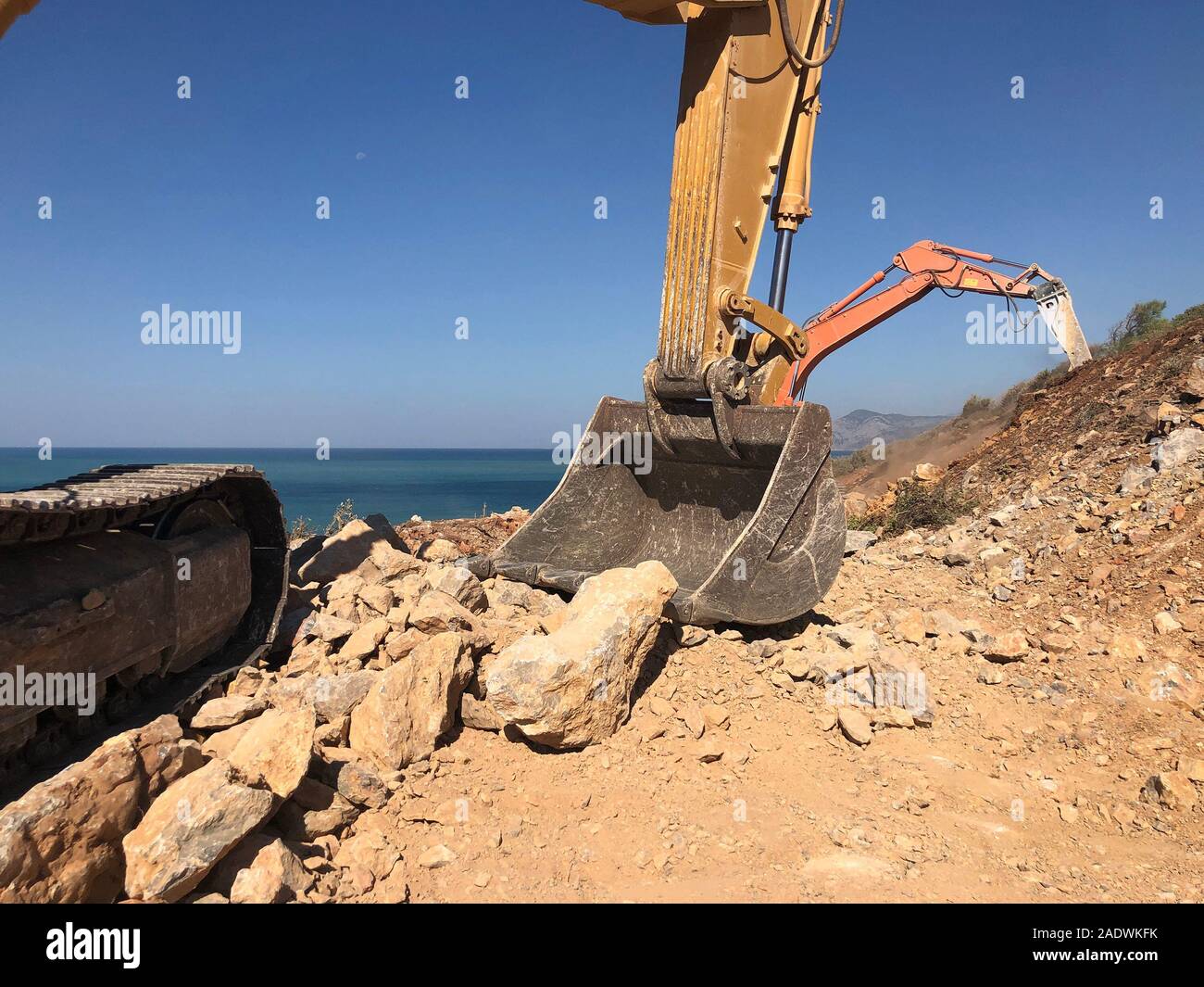 Excavators moving a rock boulders during road construction on the rocky ...