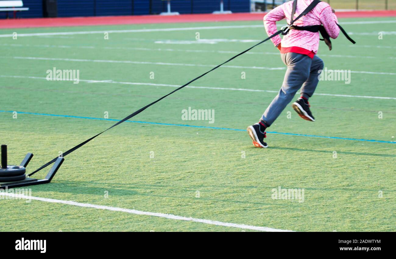 A sprinter runs on a green turf field pulling a weighted sled behind ...
