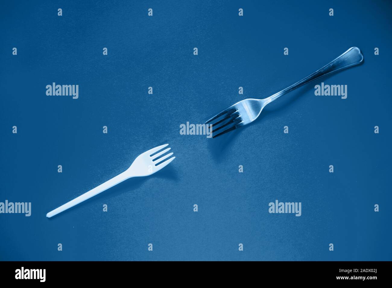 A plastic fork vs metal one on a blue background. The concept of ...