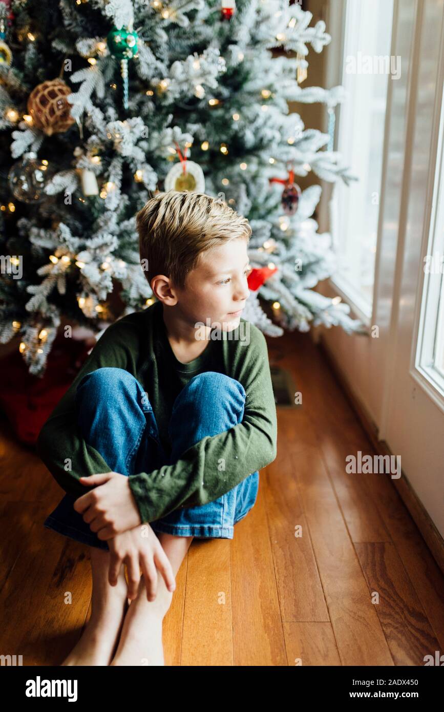 Young boy looking out window next to Christmas tree Stock Photo - Alamy