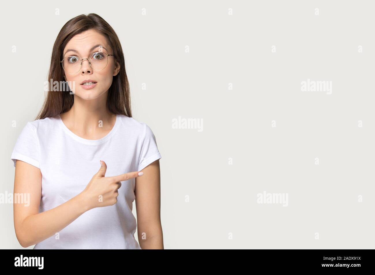 Confused young woman showing aside with finger to copyspace place Stock ...