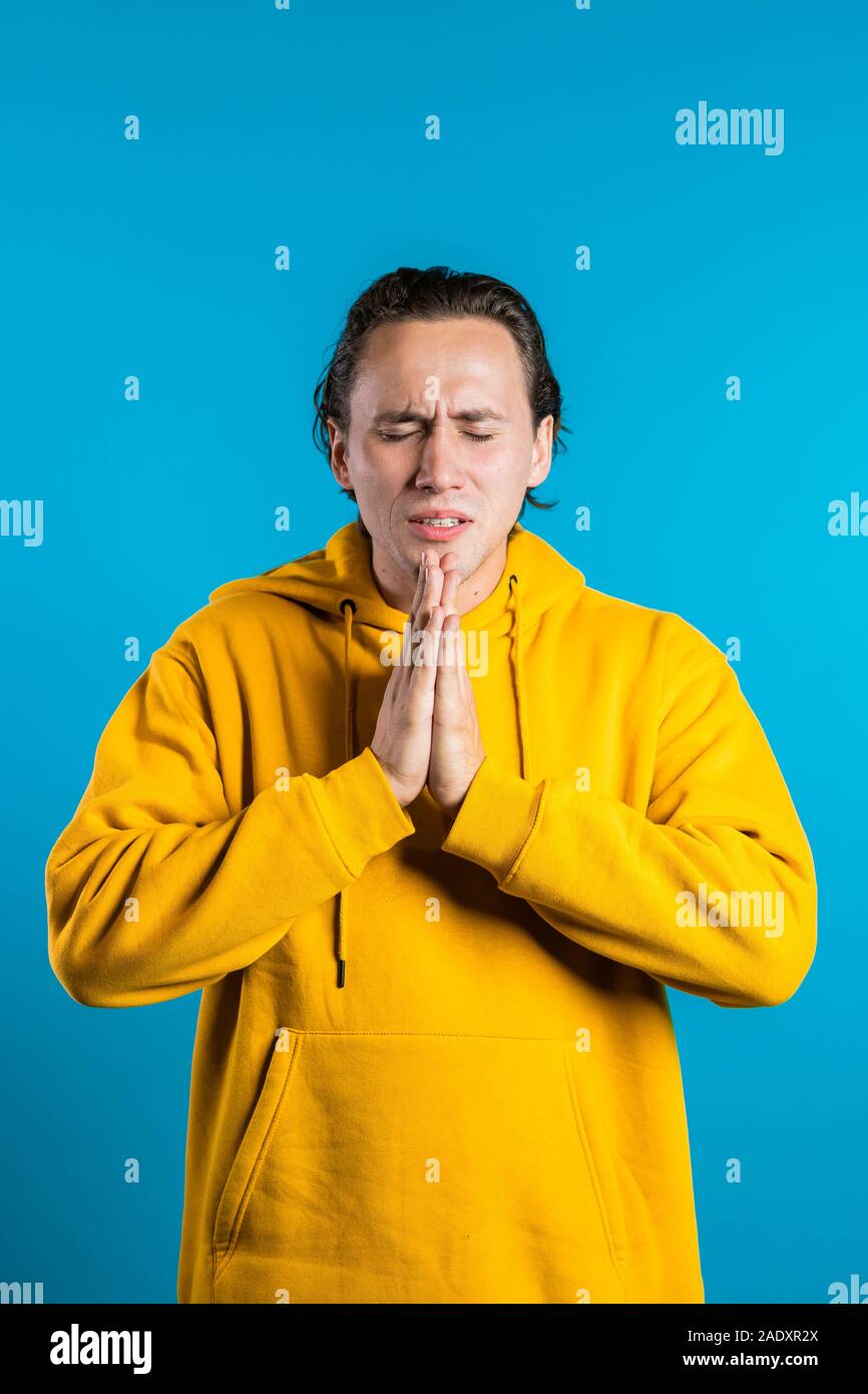 Handsome man in yellow hoodie praying over blue background. European ...