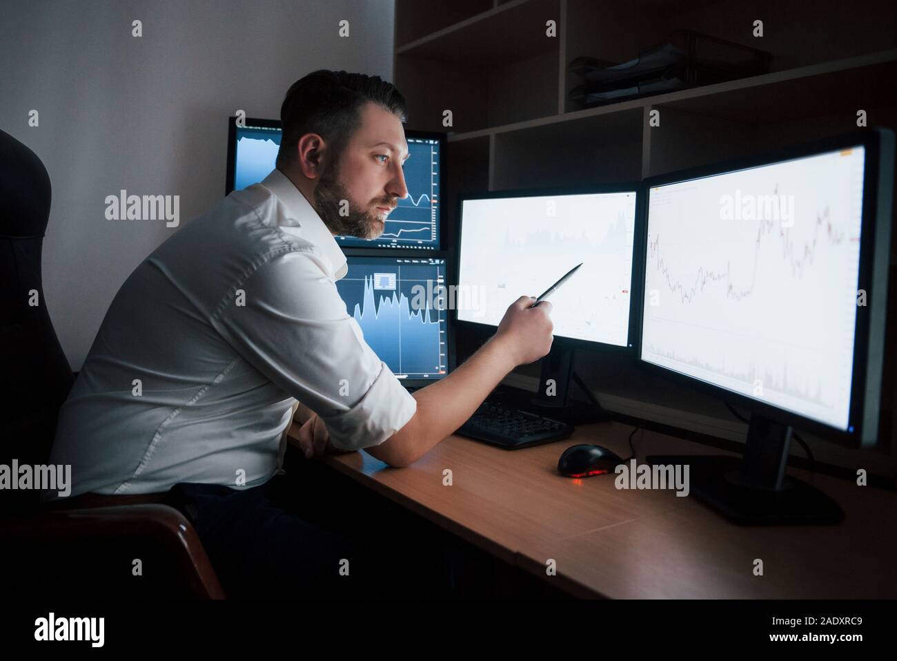 So many monitors. Bearded man in white shirt works in the office with ...