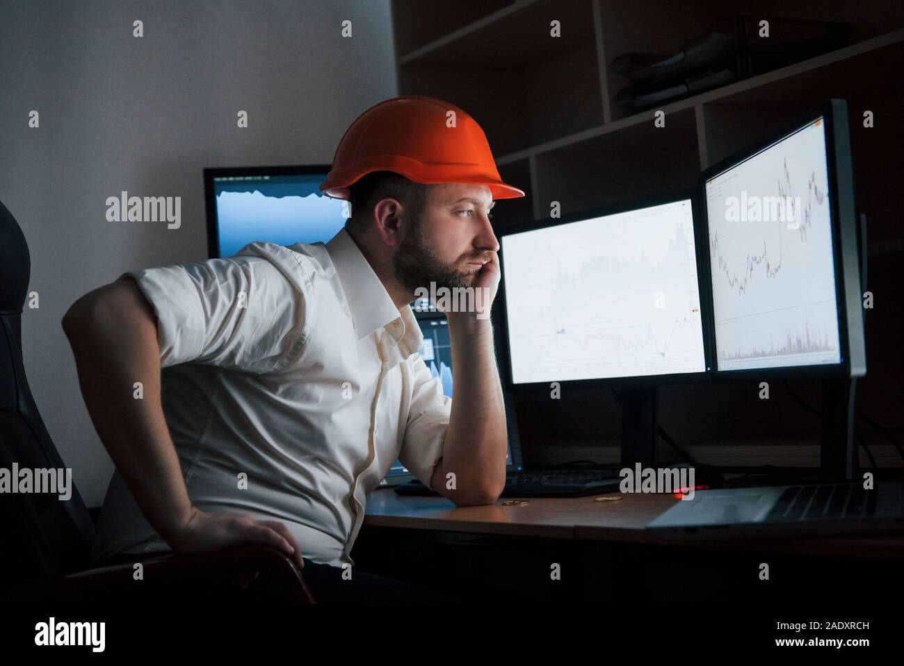 Adult engineer. Bearded man in white shirt and red safety helmet works ...