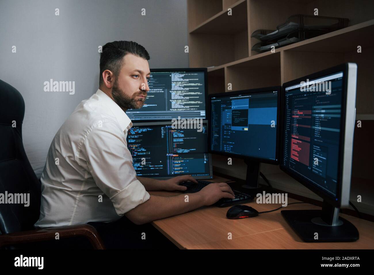 Program codes is everywhere. Bearded man in white shirt works in the ...