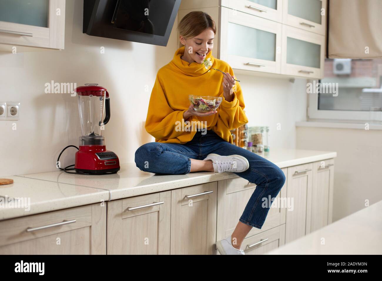 Happy young lady sitting on the countertop and enjoying her salad Stock ...