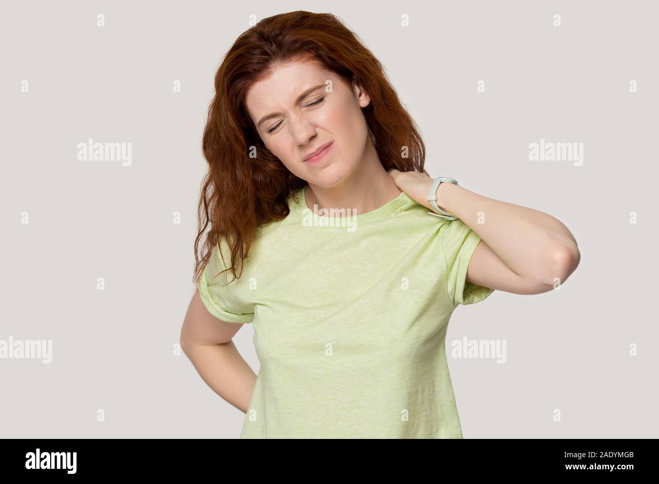 Studio portrait young red-haired woman suffering from strong back pain ...