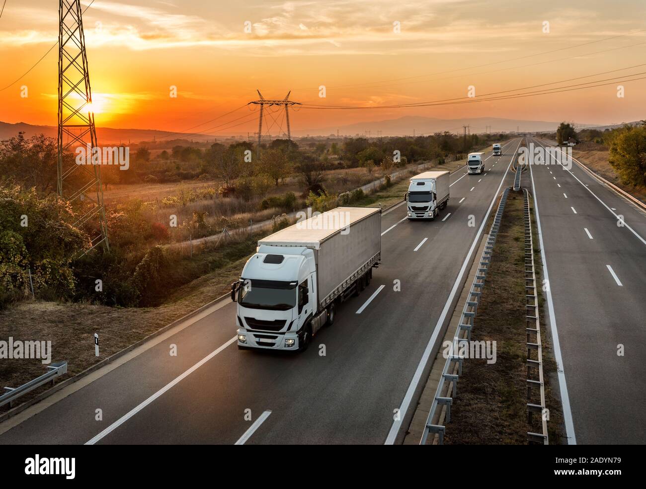 Convoy of blue lorry trucks on a country highway under amazing orange ...