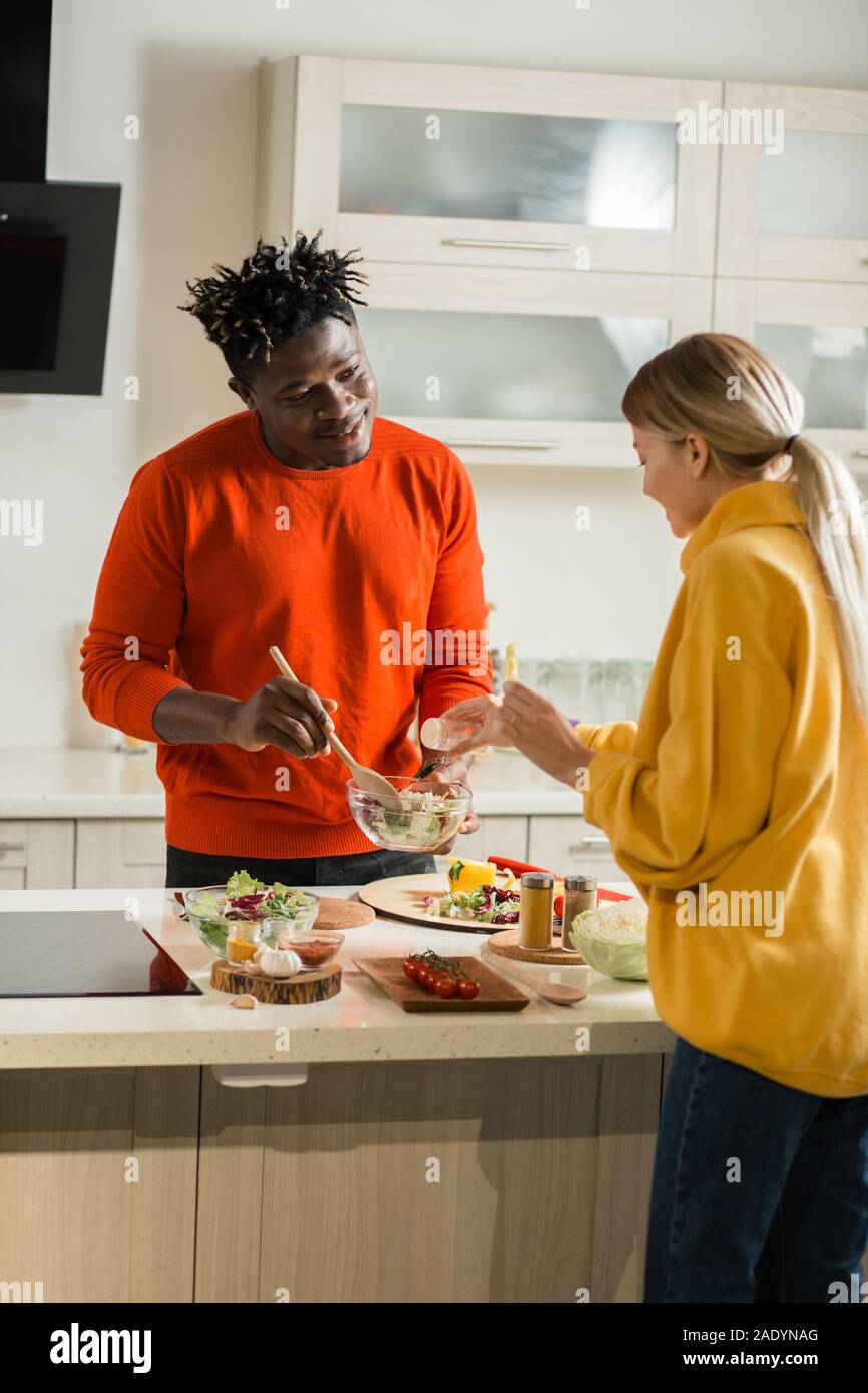 Smiling man holding salad and his girlfriend adding salt Stock Photo ...