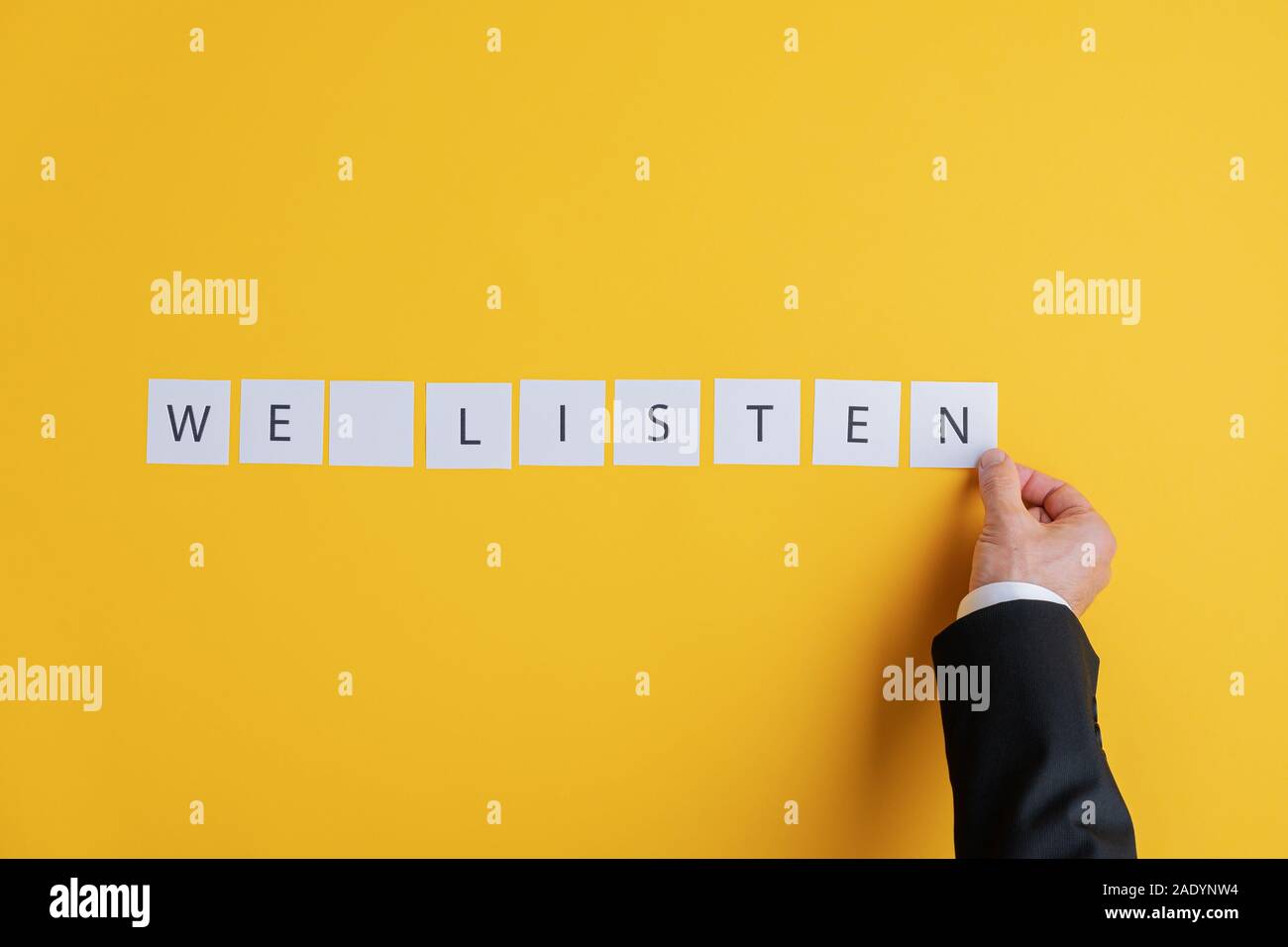 Hand of a businessman making a We listen sign spelled on white post it ...