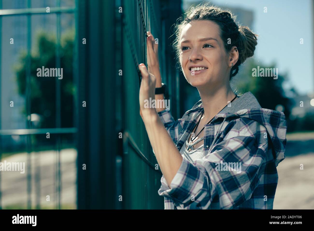 Happy lady putting hands on the chain link fence and smiling cheerfully ...