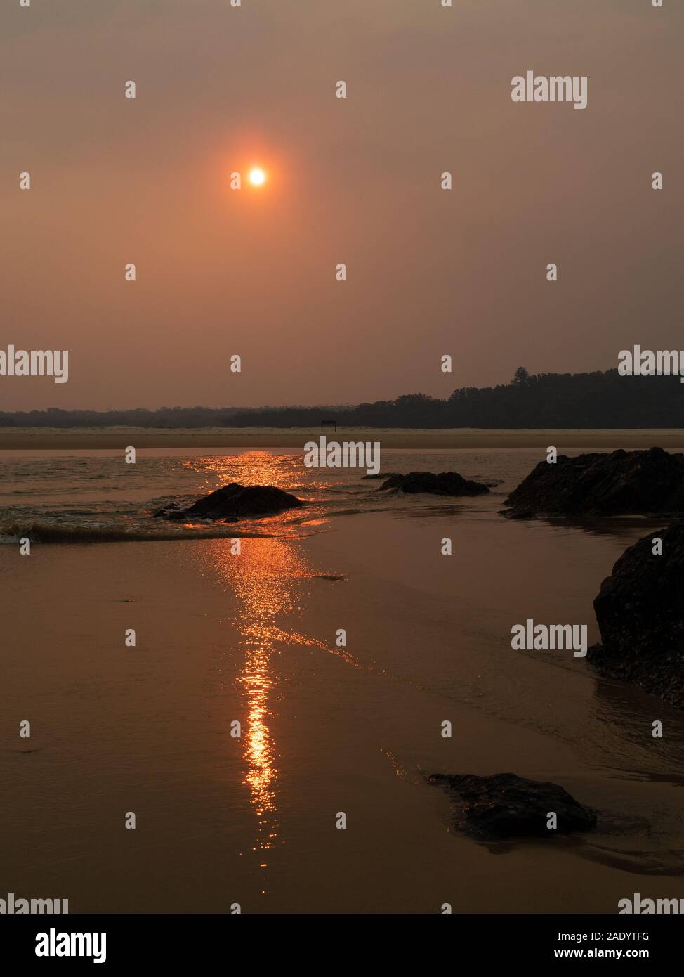 smoke haze at sunset by the beach, reflected on shiny golden orange sea ...