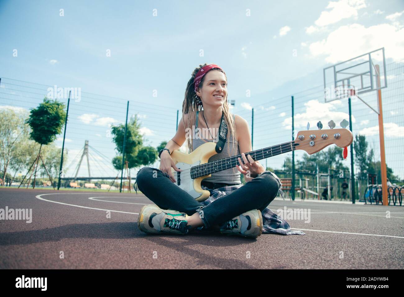 Happy musician looking glad while relaxing on sports ground with guitar ...