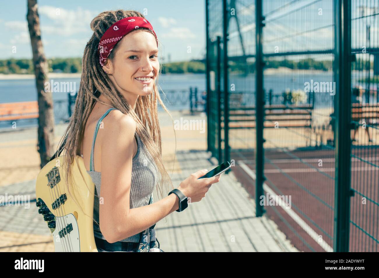 Relaxed musician walking with her guitar and smiling while turning ...