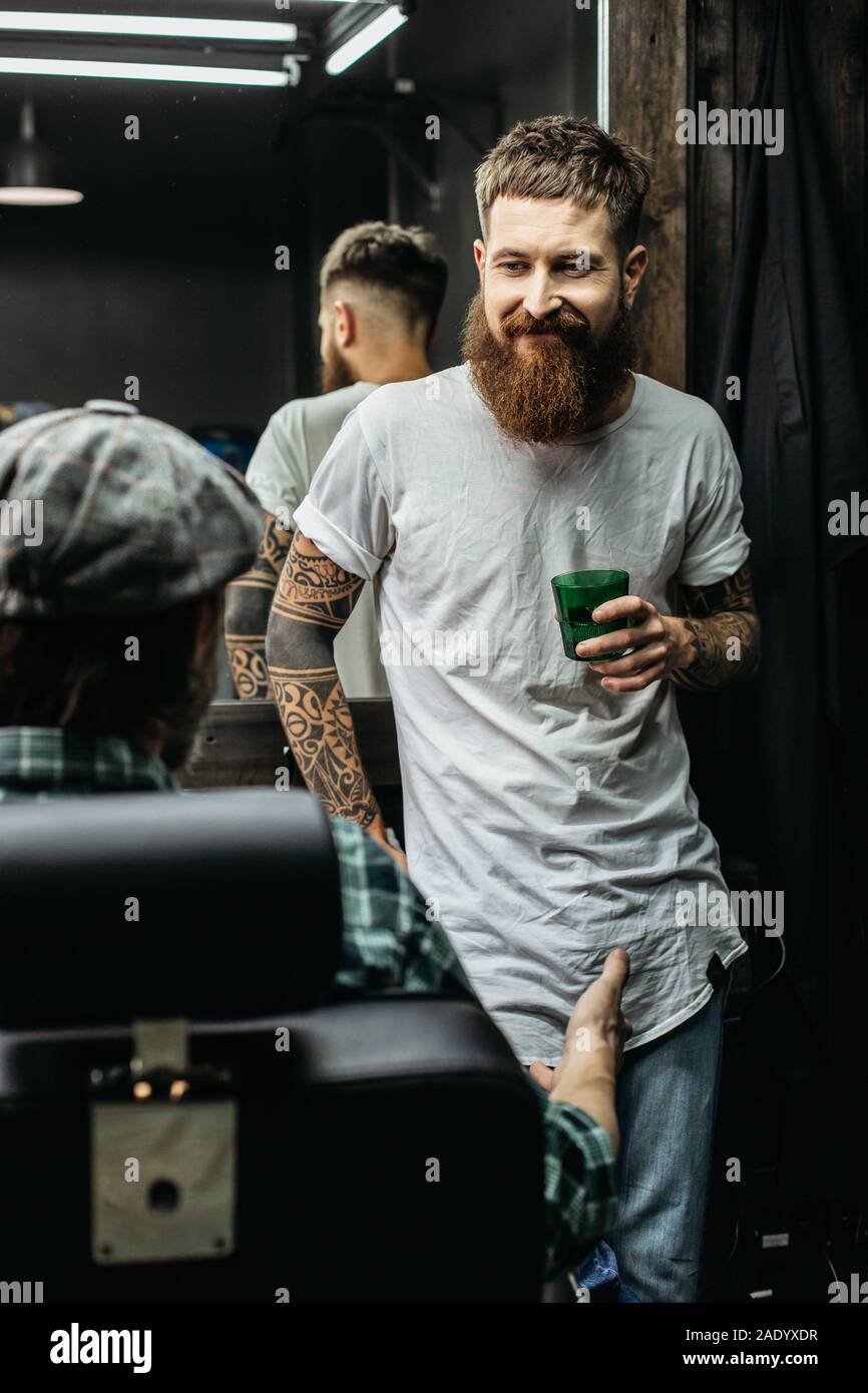 Positive handsome barber smiling to his client while standing with ... Positive handsome barber smiling to his client while standing with ...