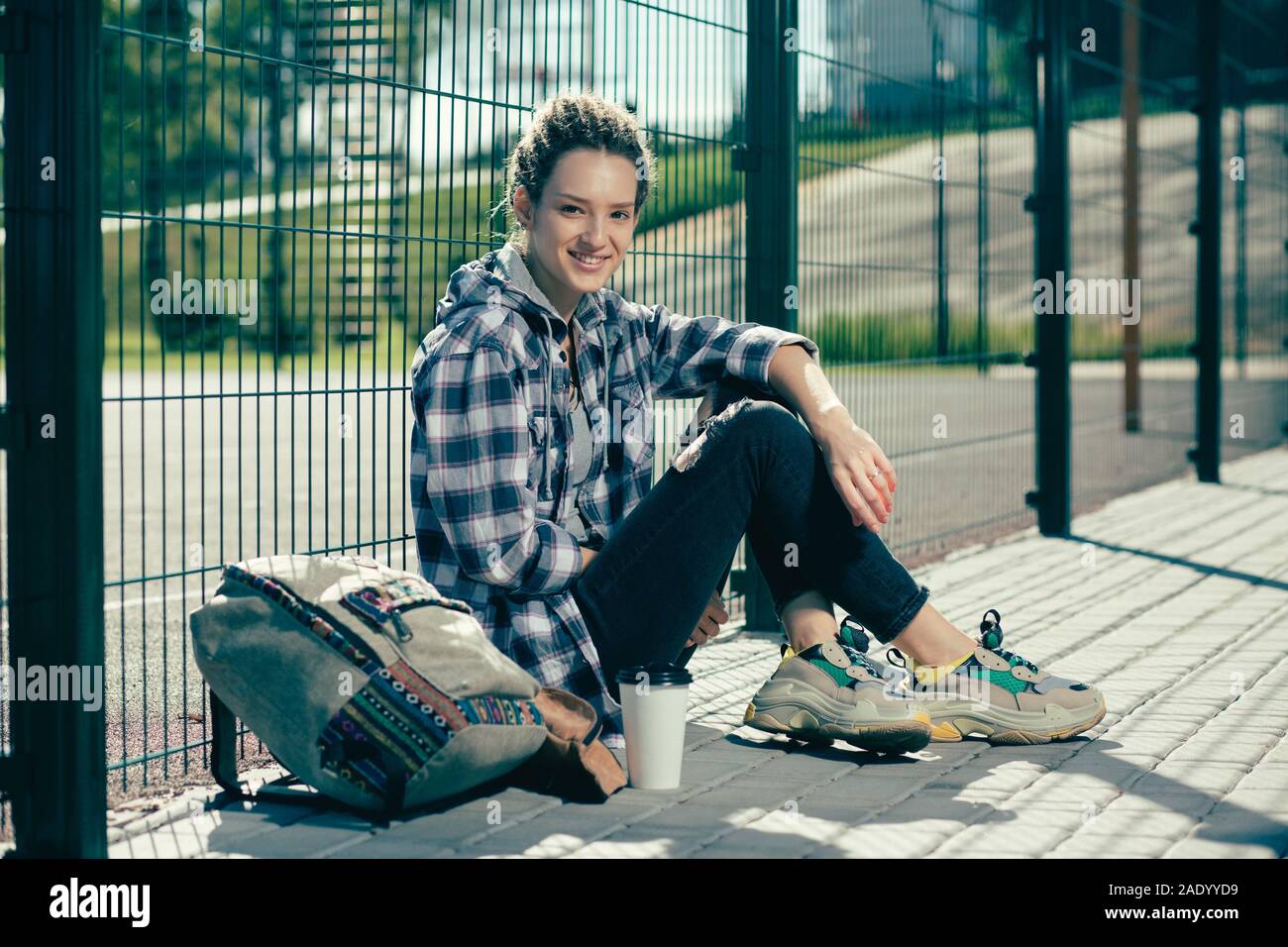 Young lady smiling while sitting on the ground by the chain link fence ...