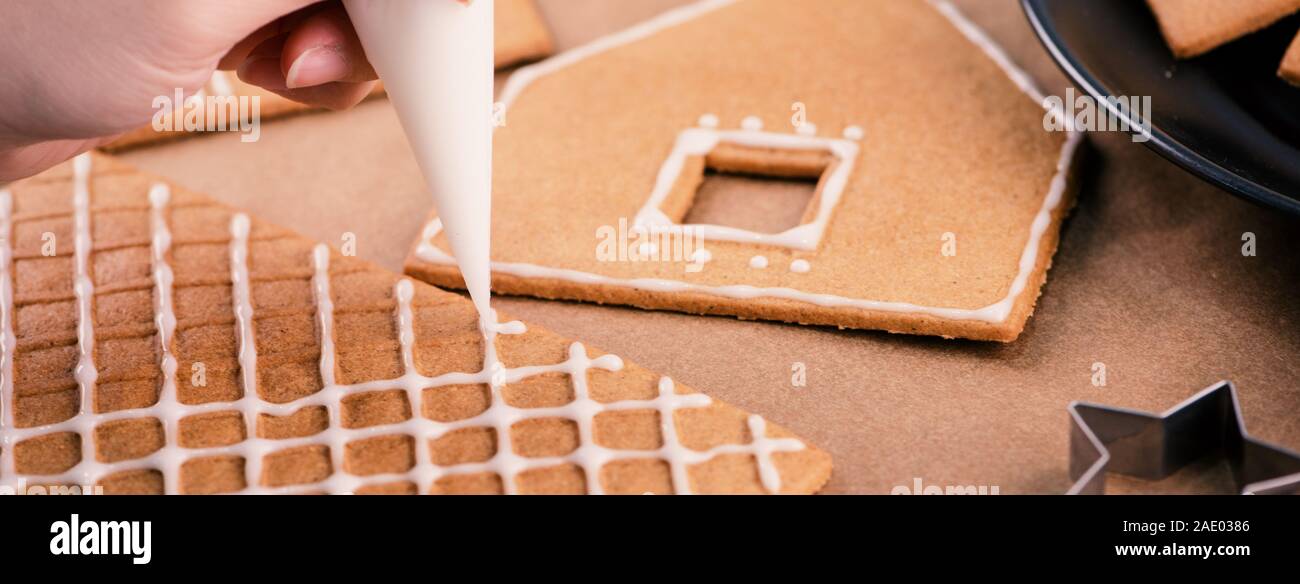 Woman is decorating gingerbread cookies house with white frosting icing ...