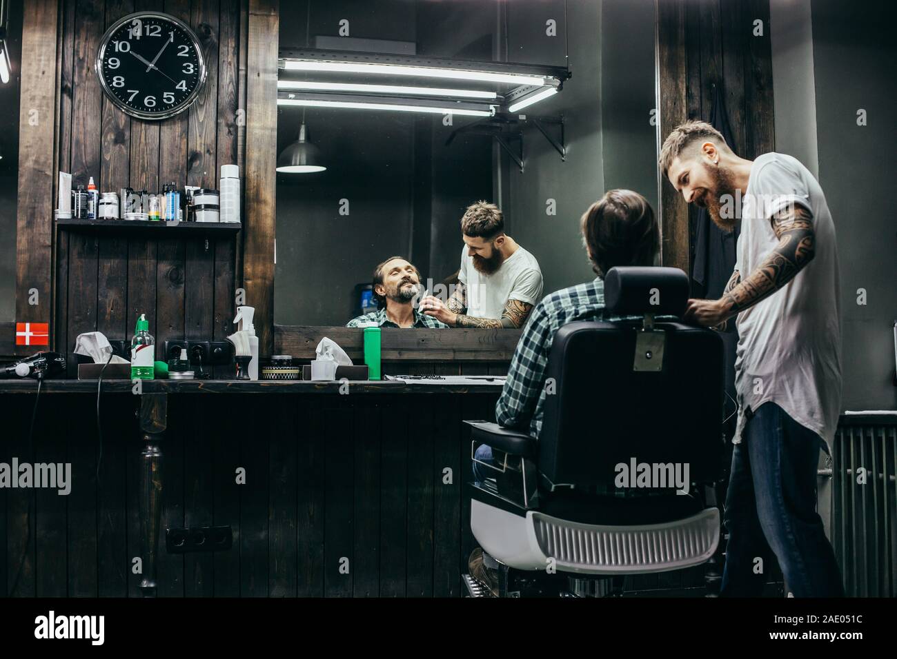 Friendly barber smiling and combing beard of his client Stock Photo - Alamy