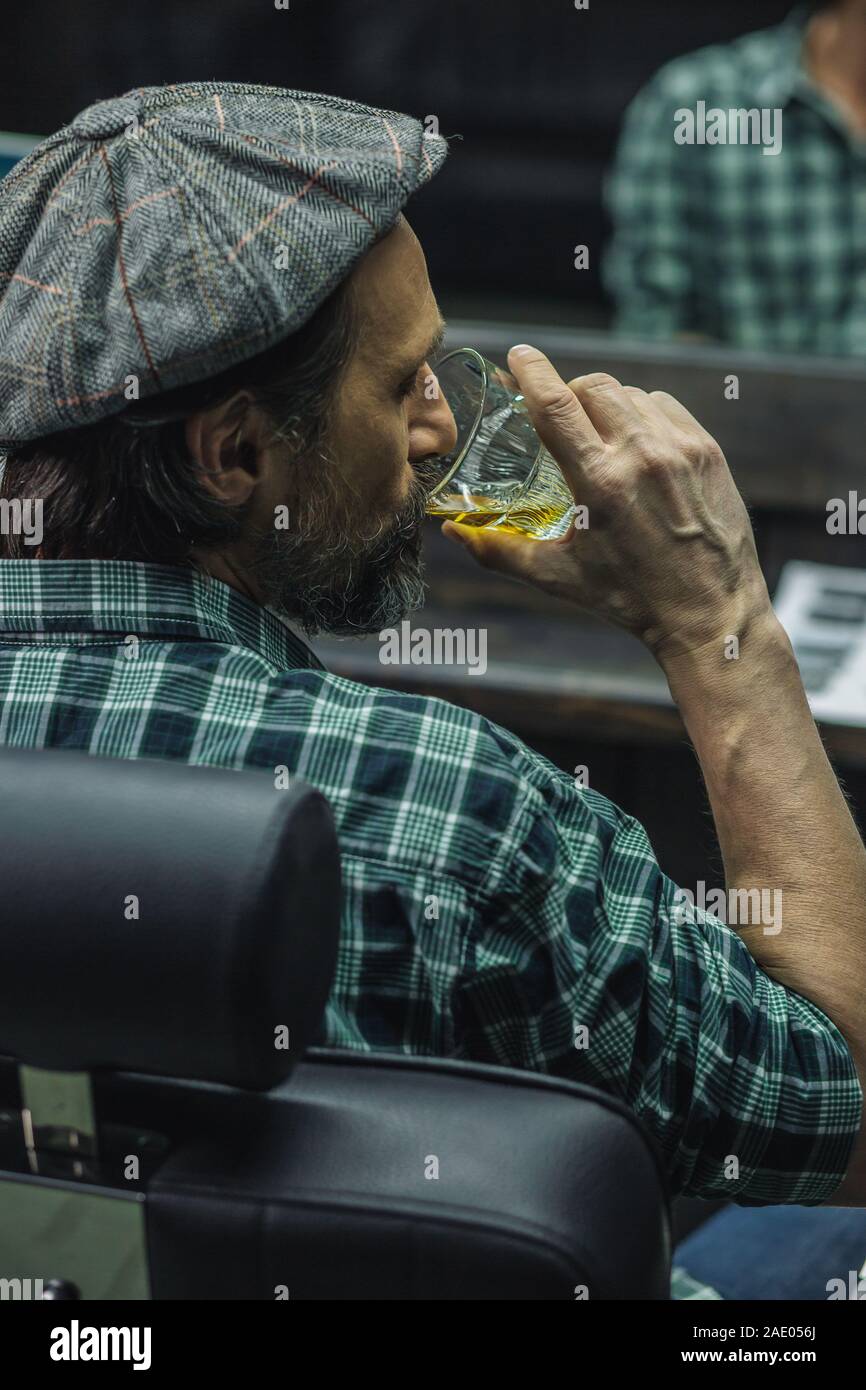 Calm man in flat hat sitting and drinking alcohol Stock Photo - Alamy