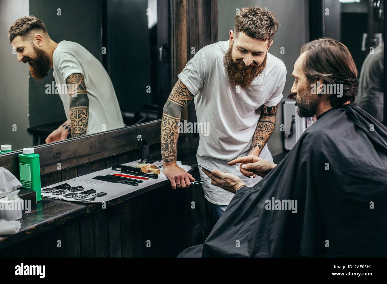 Friendly barber smiling while client showing screen of smartphone Stock ...