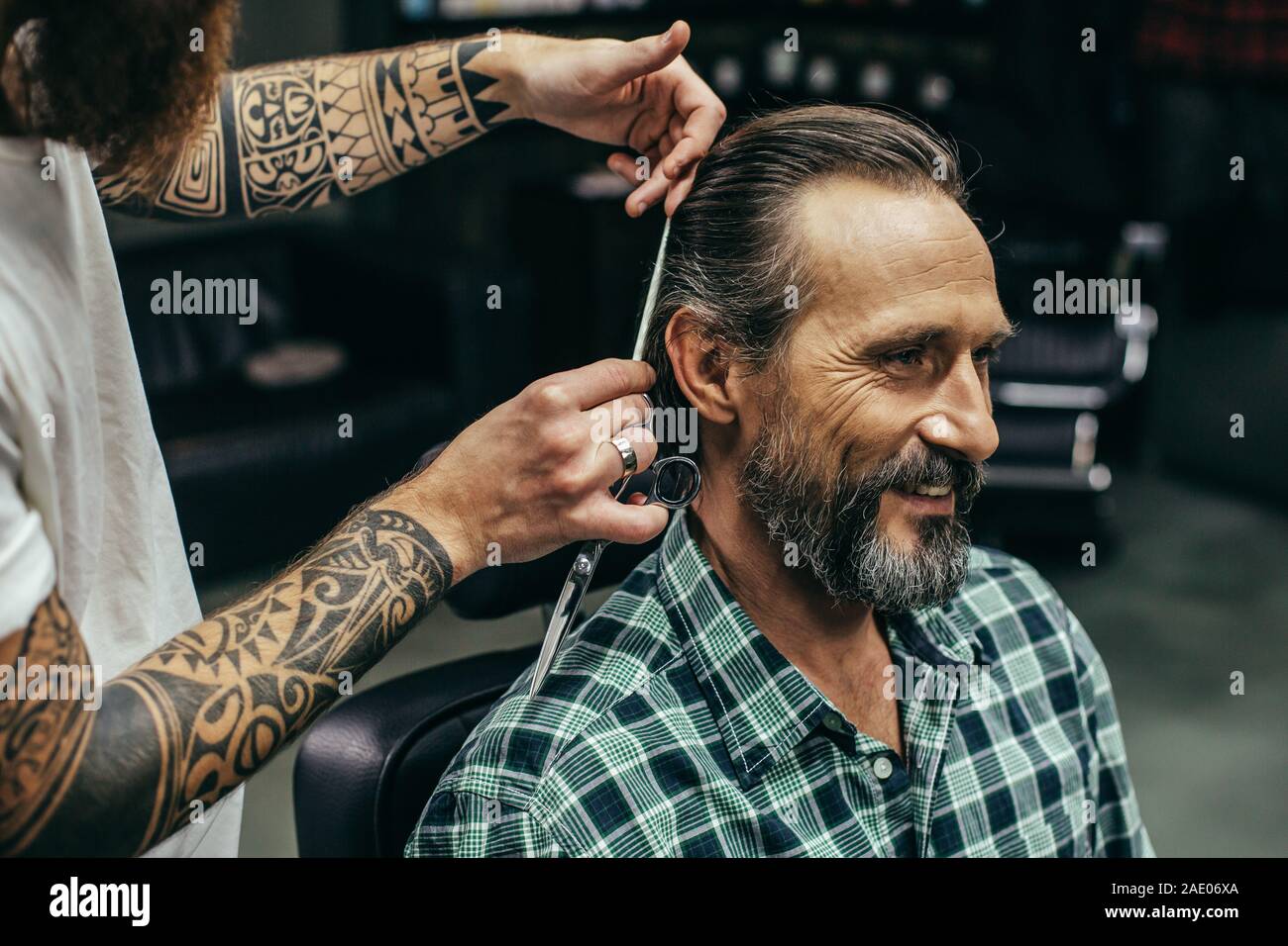 Positive man smiling and barber with tattoos doing haircut for him ... Positive man smiling and barber with tattoos doing haircut for him ...
