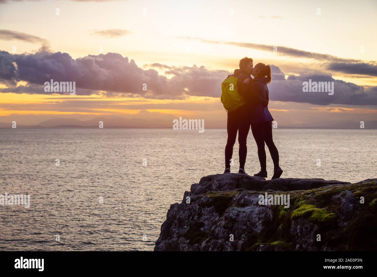 Adventurous couple kissing and standing on a rocky cliff by the Pacific ...