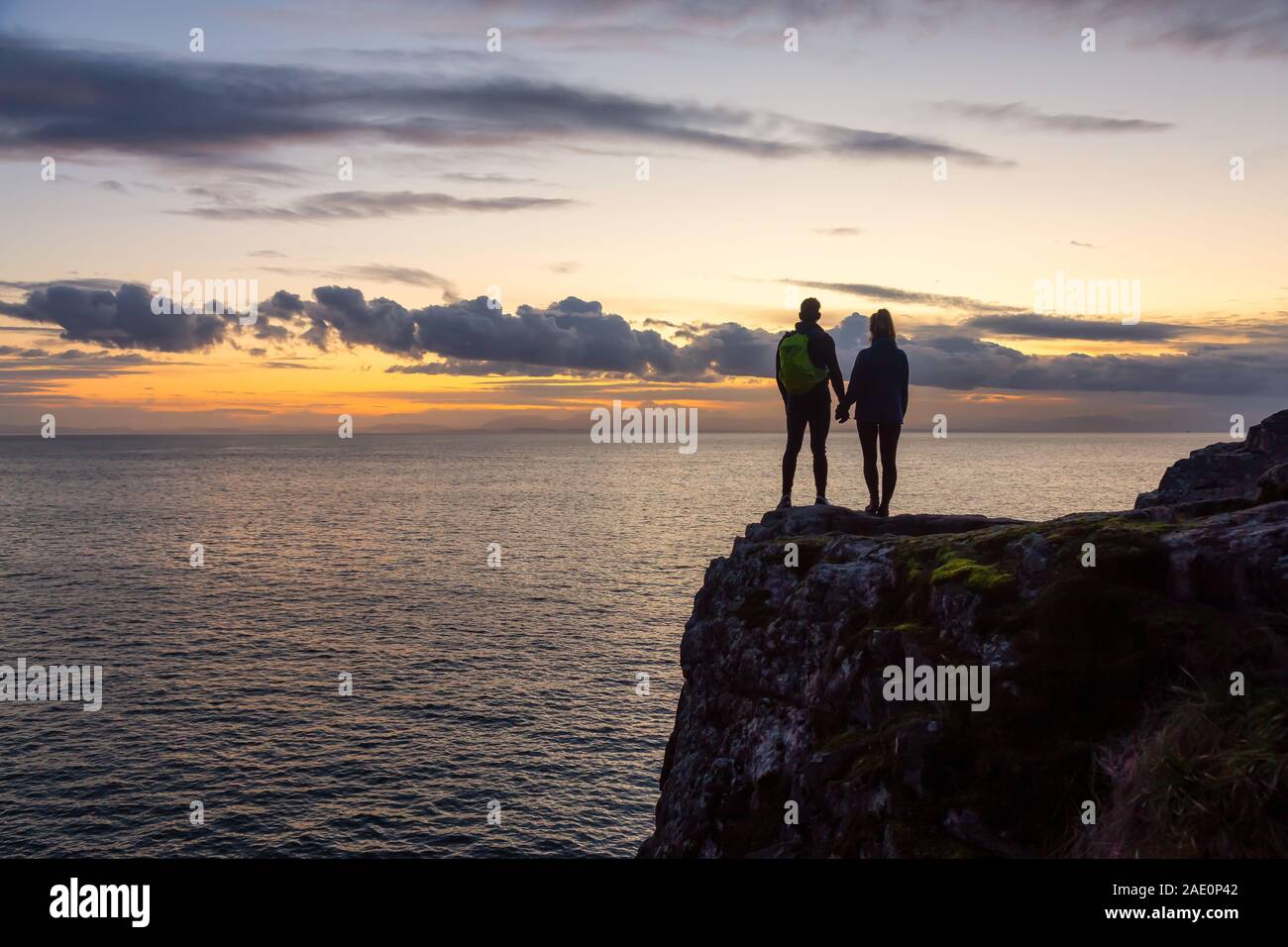 Adventurous couple holding hands and standing on a rocky cliff by the ...