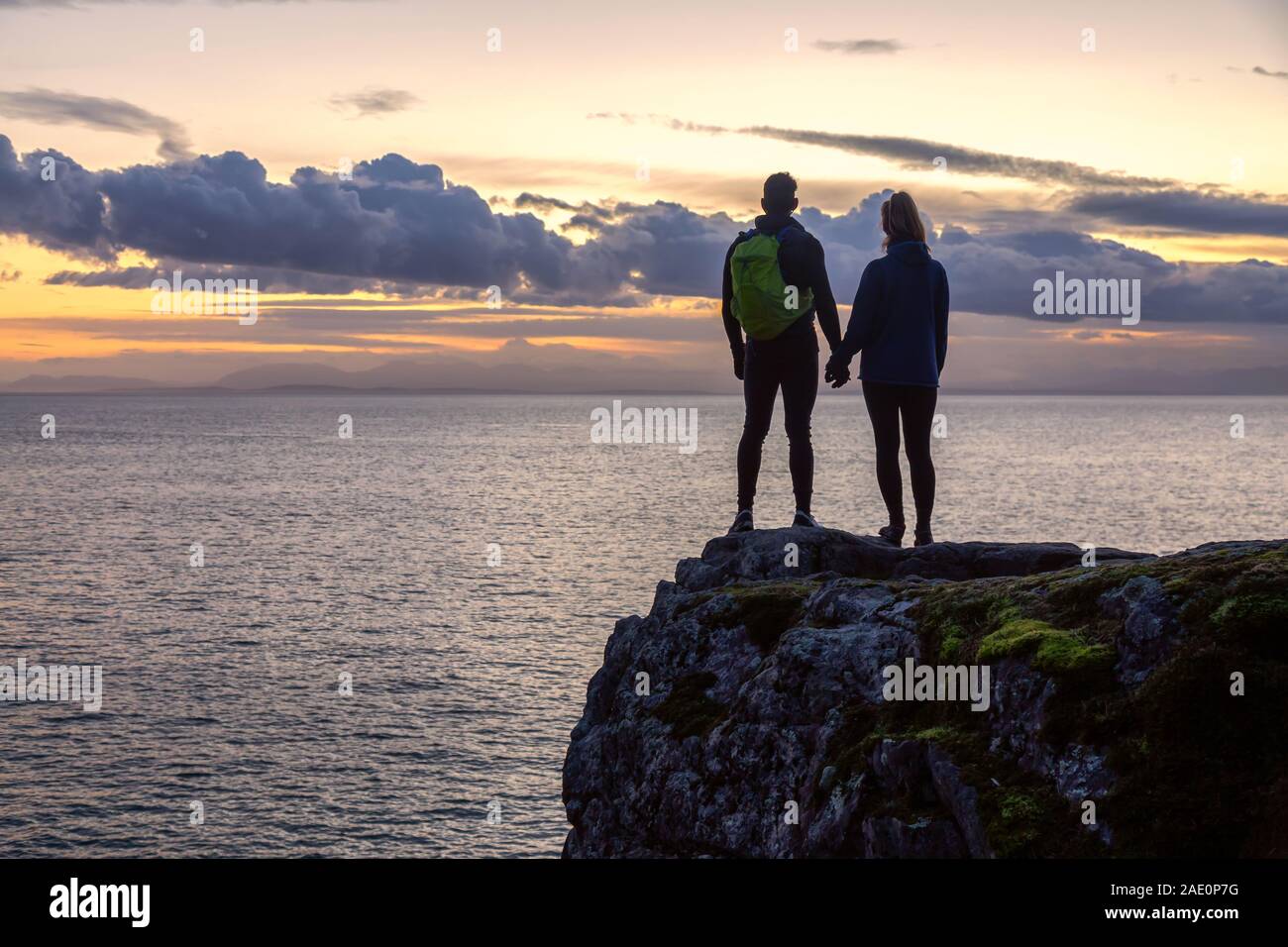 Adventurous couple holding hands and standing on a rocky cliff by the ...