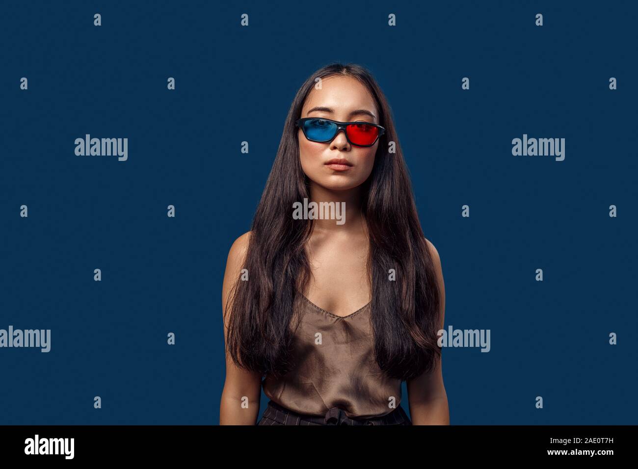 Freestyle. Young woman in 3d glasses standing isolated on dark blue looking camera serious Stock ...