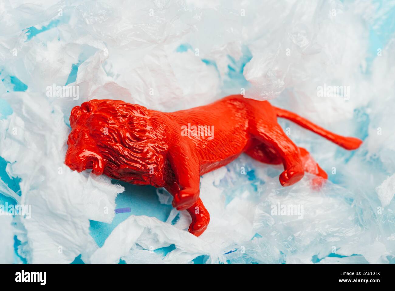 Red toy lion on plastic garbage on blue background, animal welfare ...