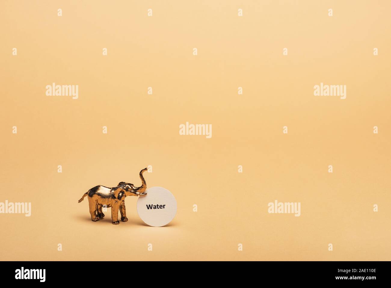 Golden toy elephant with lettering water on card on yellow background ...