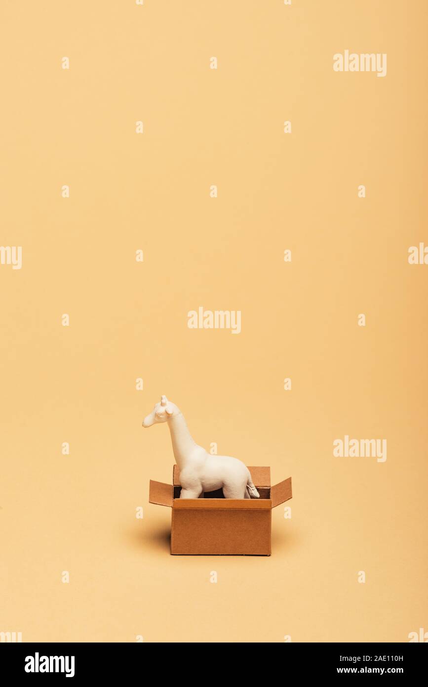 White toy giraffe in cardboard box on yellow background, animal welfare ...