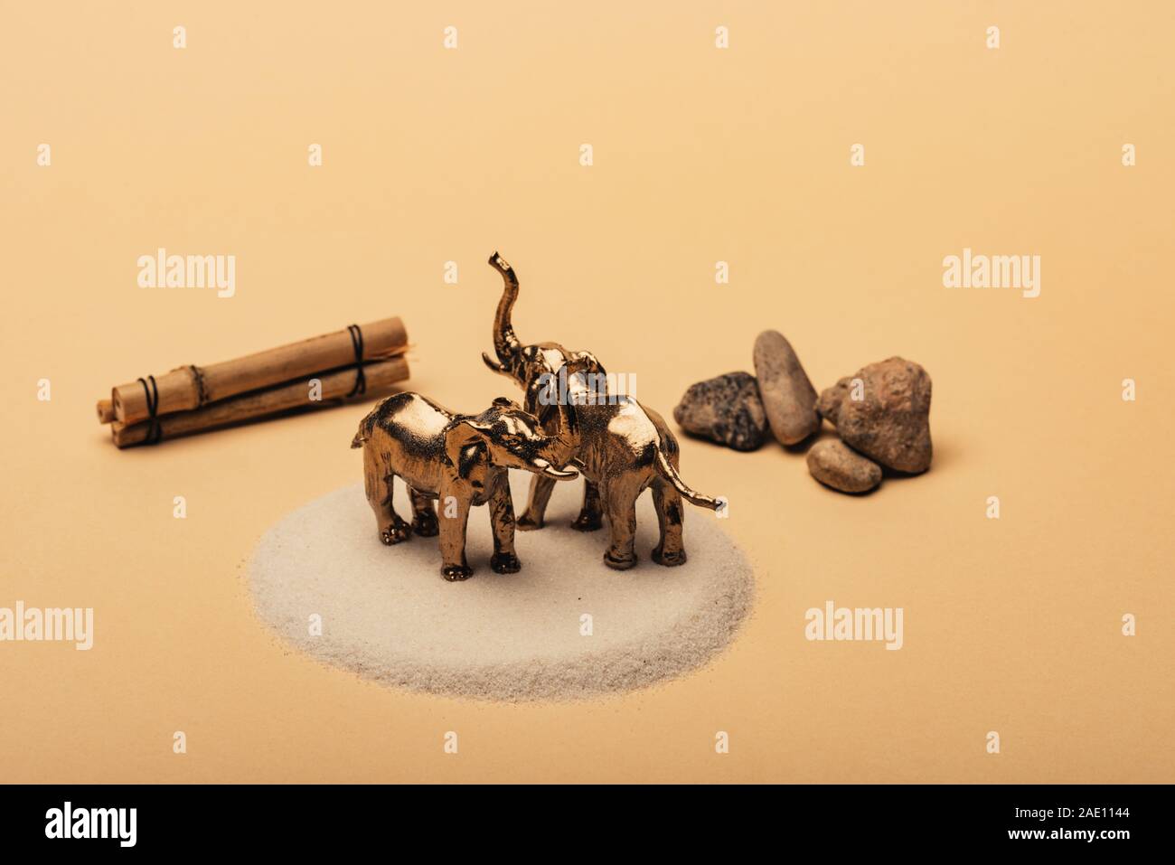 Toy elephants on sand with stones and wooden sticks on yellow ...