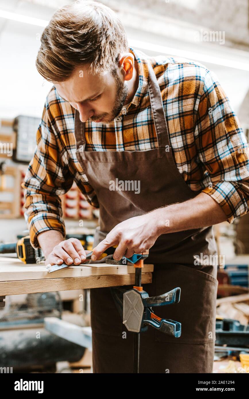 bearded carpenter in brown apron carving wood in workshop Stock Photo ...