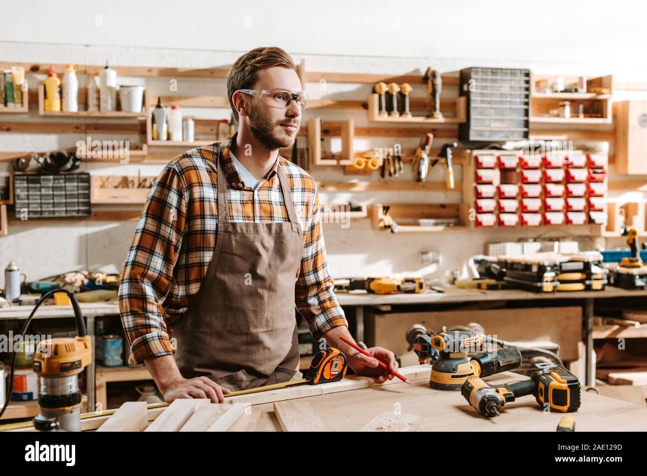 handsome carpenter in goggles standing near table and equipment Stock ...