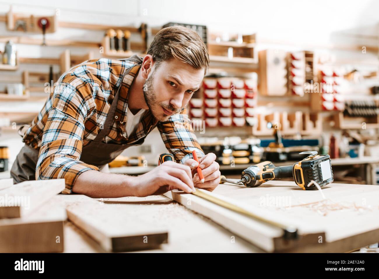 selective focus of handsome woodworker holding pencil while measuring ...