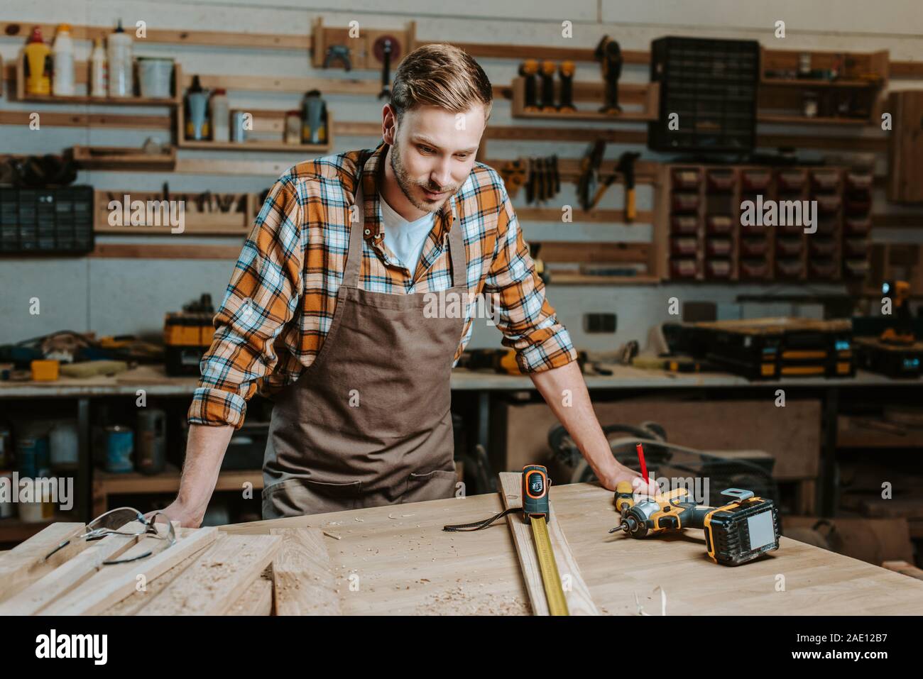 handsome woodworker looking at table with wooden planks and measuring ...