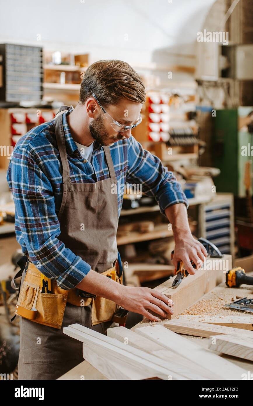 selective focus of carpenter in goggles holding pliers near wooden ...