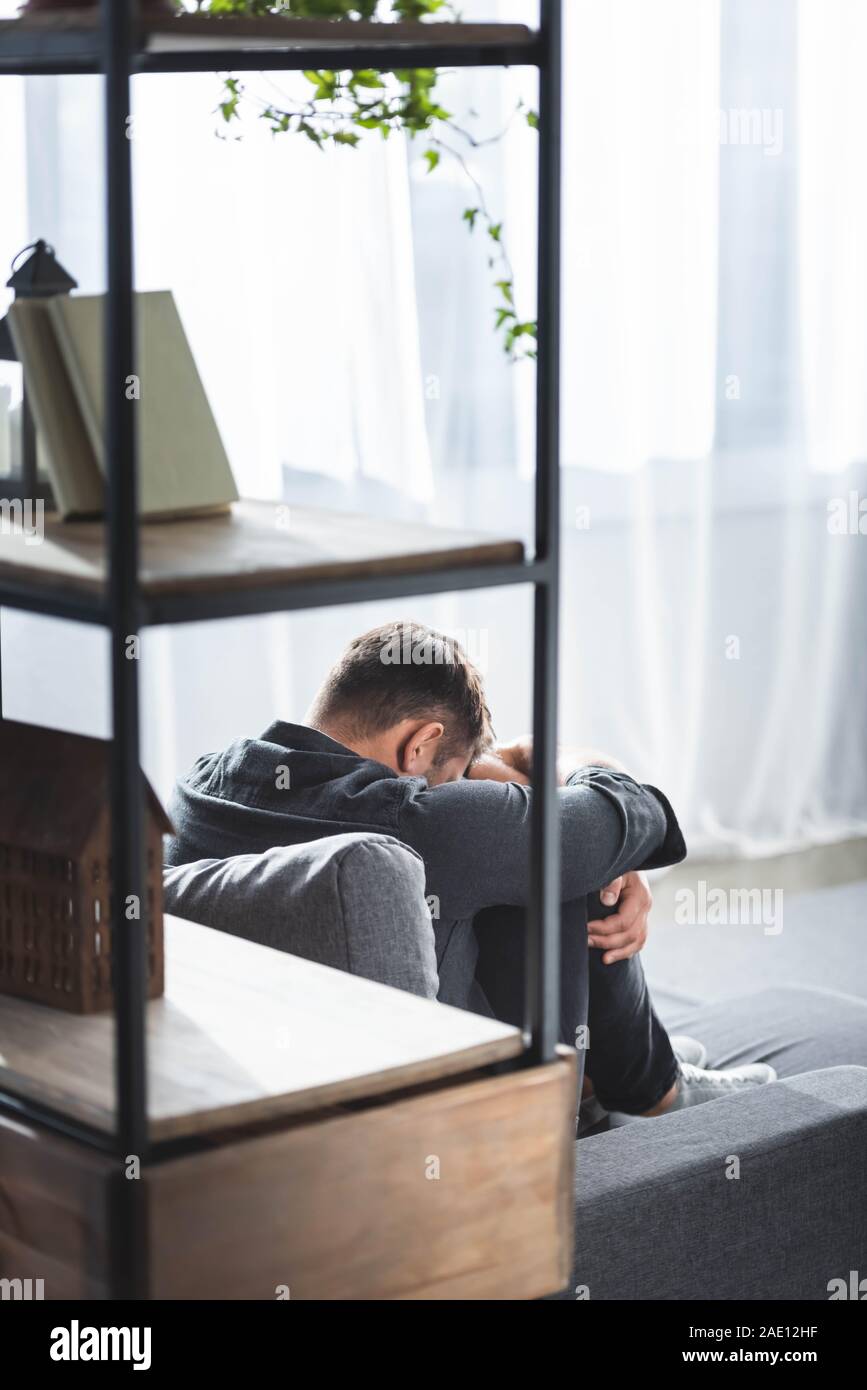 back view of man with panic attack crying and hugging legs in apartment ...