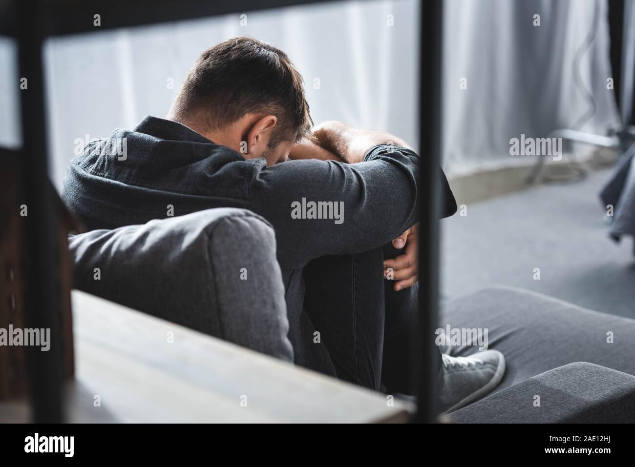 back view of man with panic attack crying and hugging legs in apartment ...