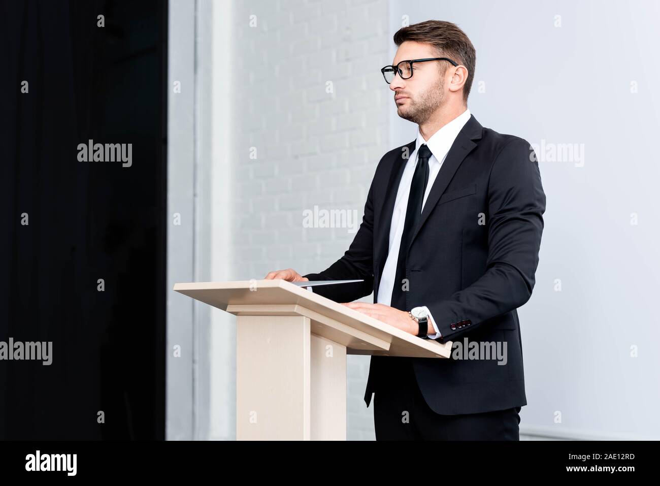 businessman in suit standing at podium tribune and looking away during ...