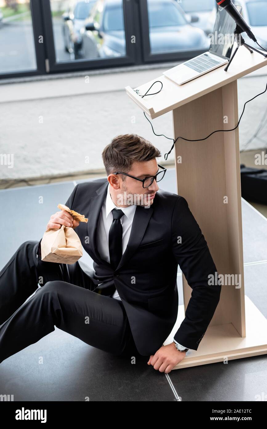 scared businessman in suit holding paper bag and hiding behind podium ...