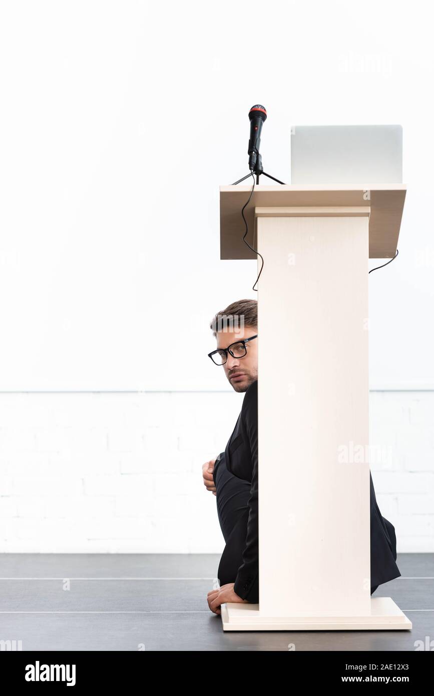 scared businessman in glasses hiding behind podium tribune during ...