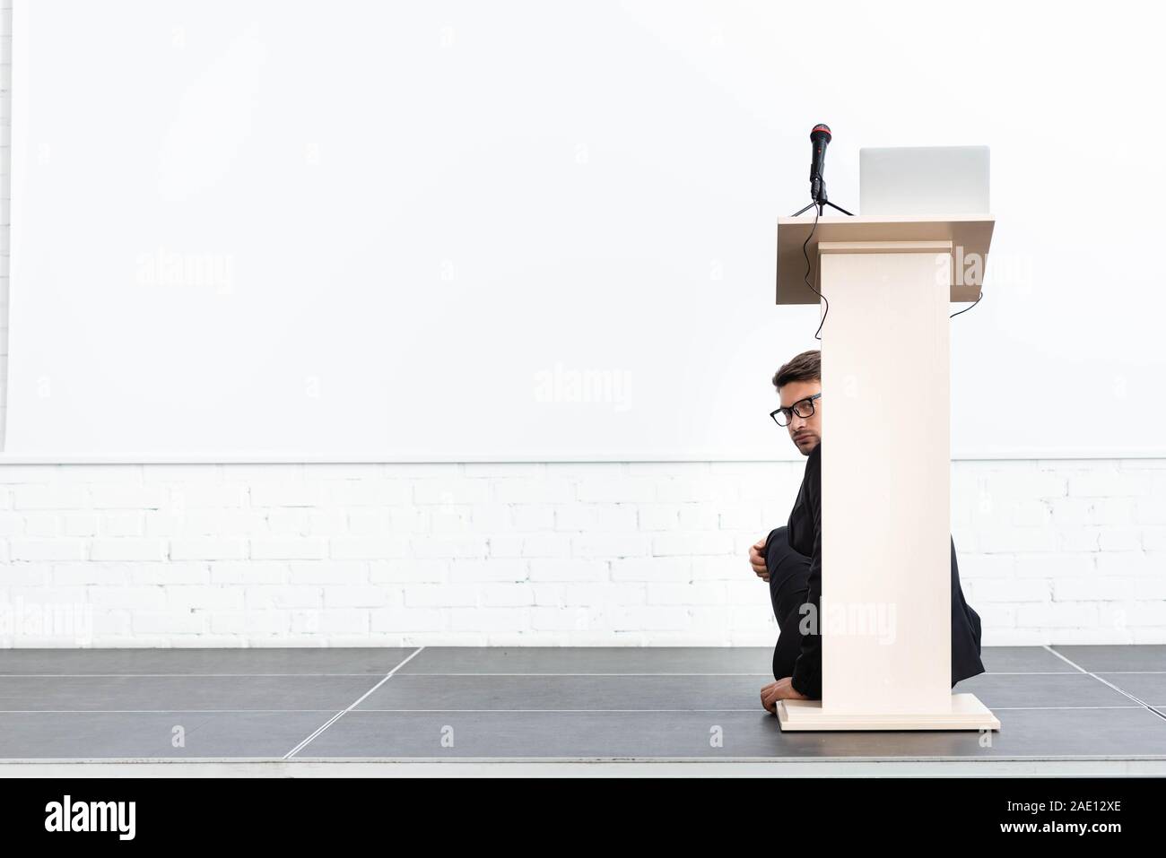 scared businessman in glasses hiding behind podium tribune during ...